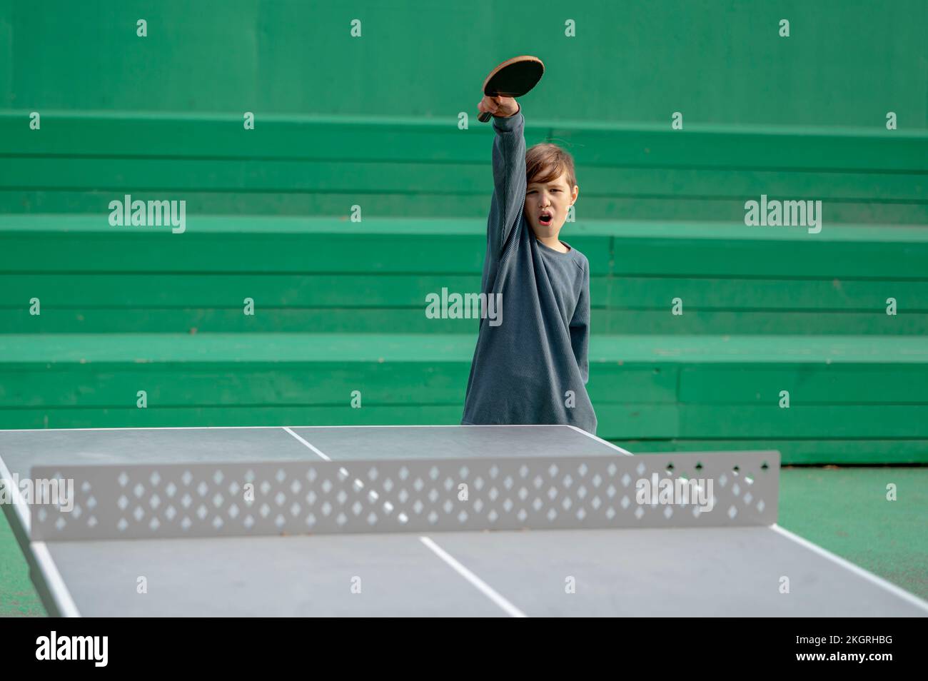 Boy holding table tennis racket screaming in front of green wall Stock ...