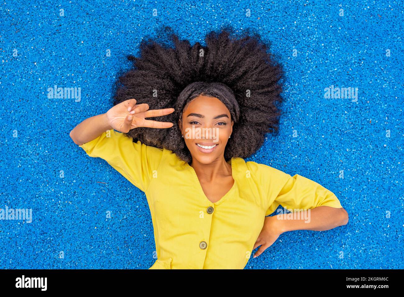 Happy woman gesturing peace sign and lying on blue basketball court ...