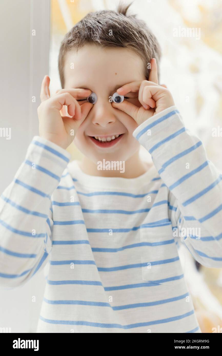 Happy boy holding small googly eyes over face at home Stock Photo - Alamy