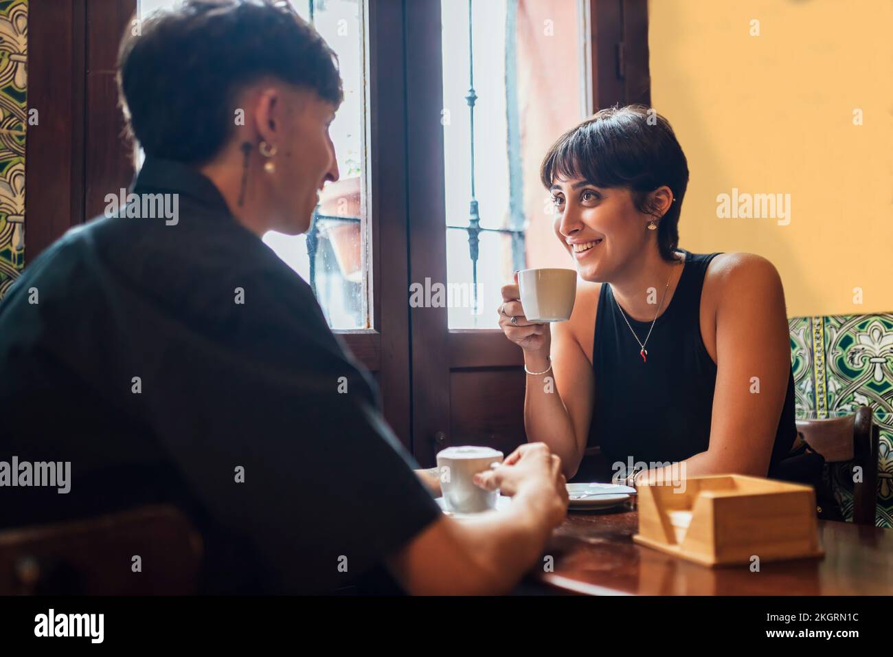 Happy young woman holding coffee cup talking with boyfriend in cafe ...