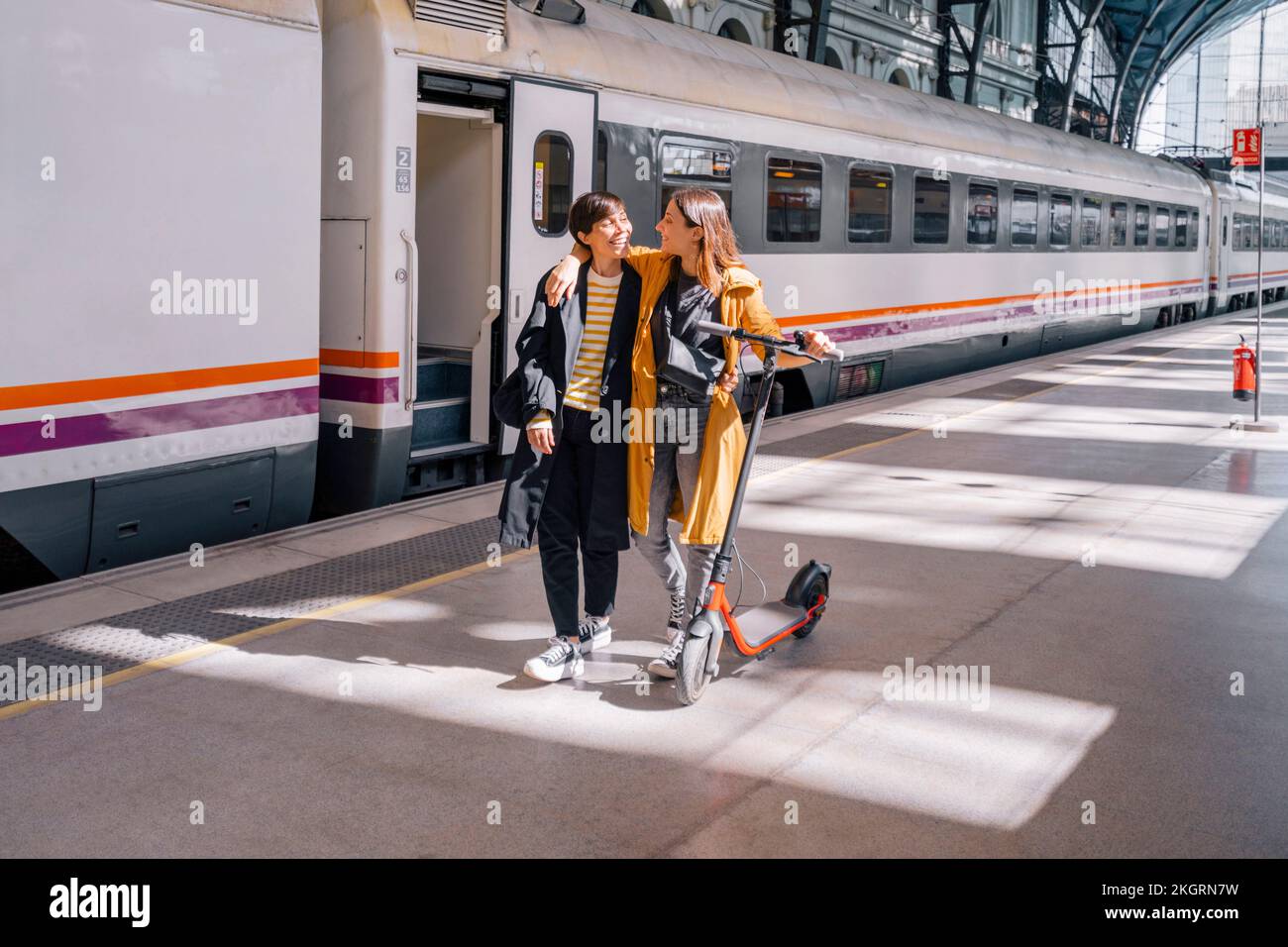 Happy friends walking with push scooter at railroad station Stock Photo ...