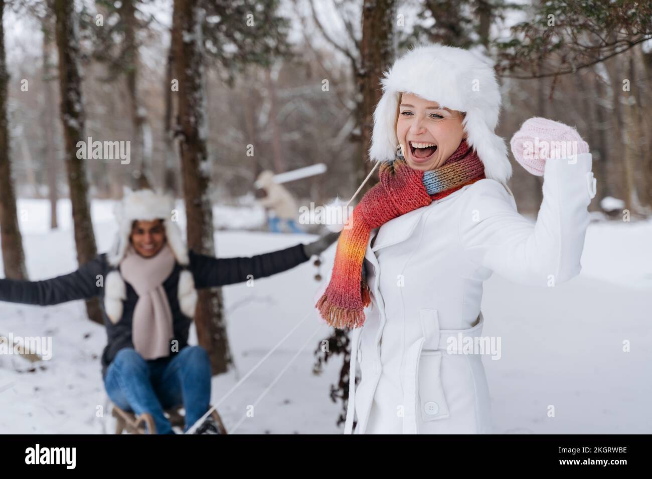 Happy woman flexing muscles with man sitting on sled in snow Stock ...