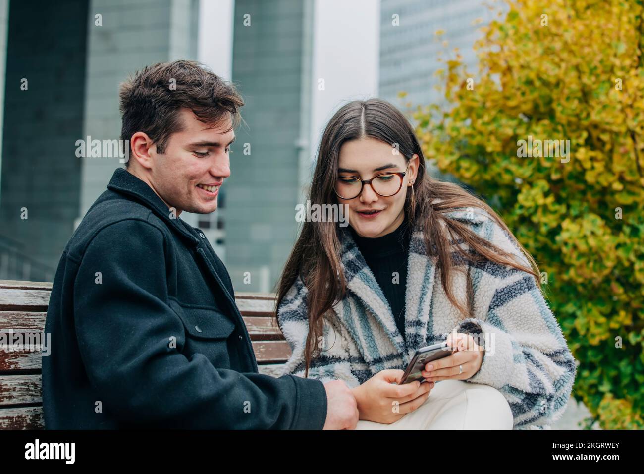 Girlfriend sharing mobile phone with boyfriend on bench Stock Photo - Alamy
