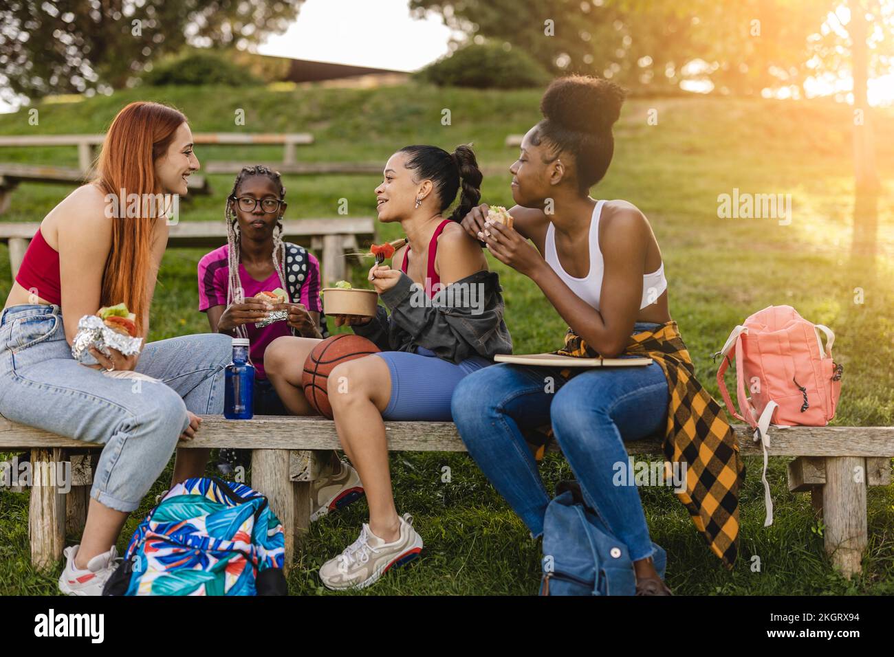 Happy friends having snack sitting on bench at park Stock Photo - Alamy