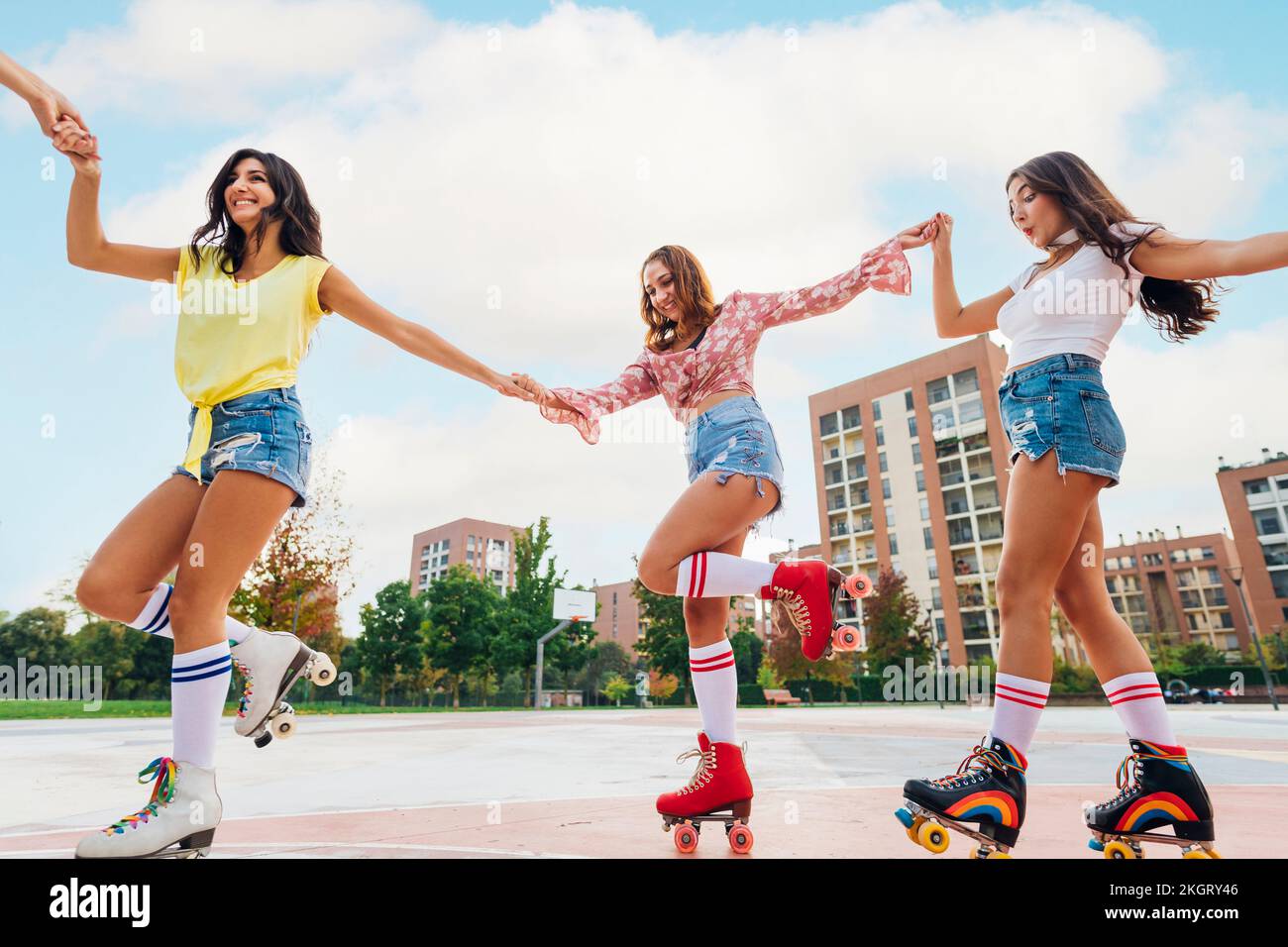Happy friends holding hands and roller skating at sport court Stock ...