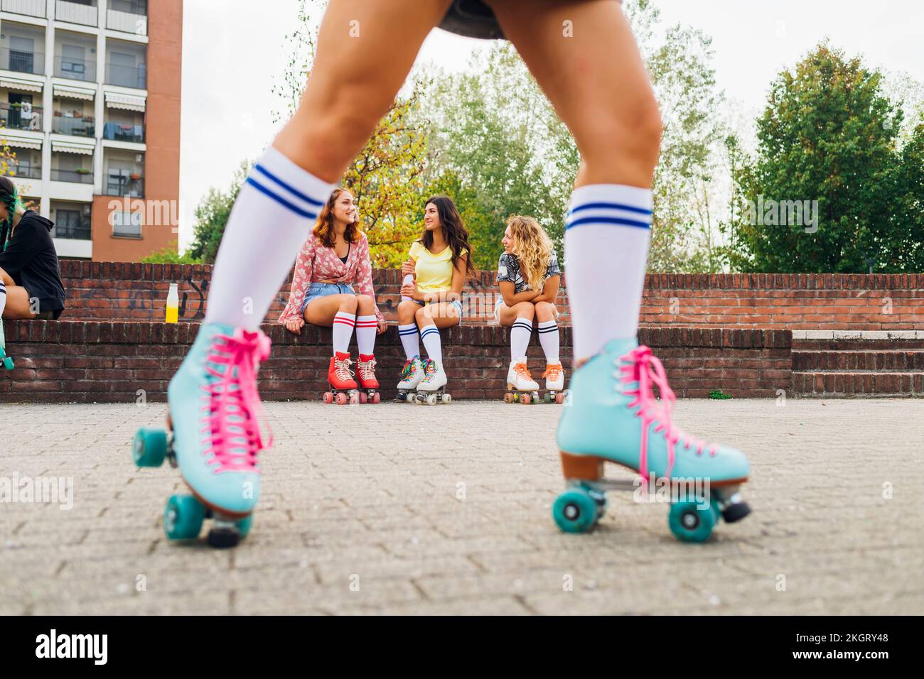 Friends sitting on wall seen through legs of woman roller skating at ...