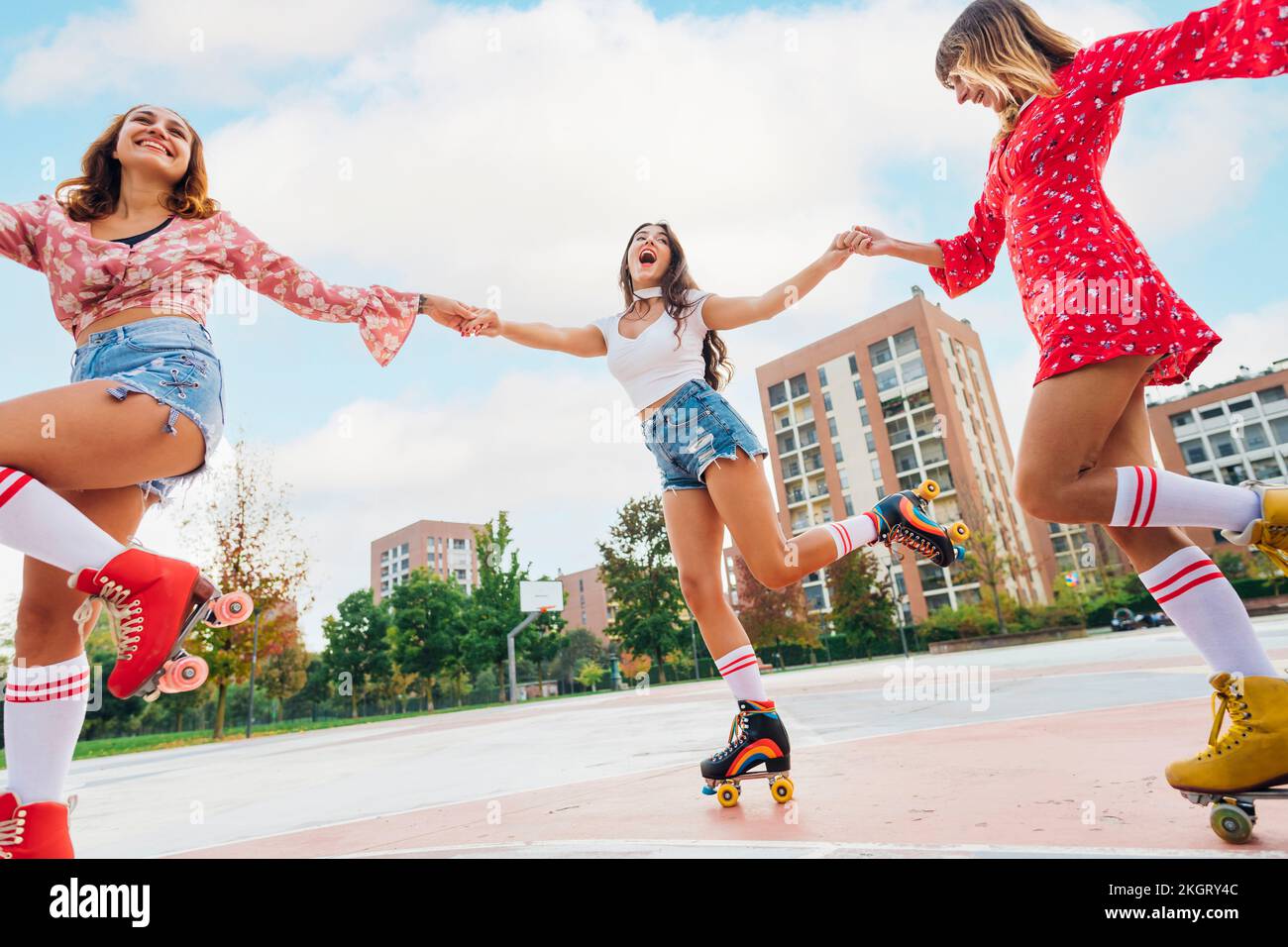 Happy friends holding hands practicing roller skating at sports court ...