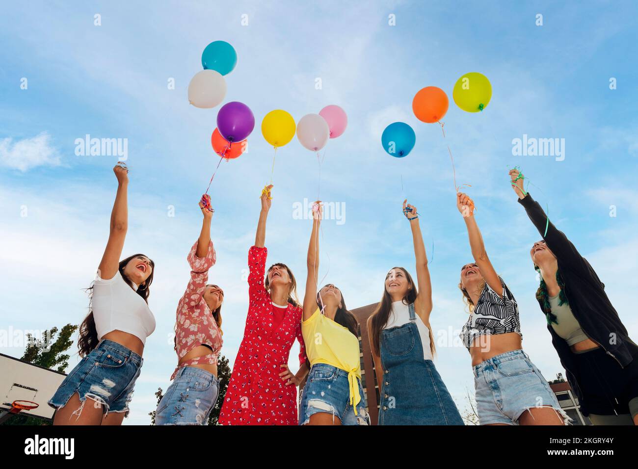 Happy friends with hands raised holding colorful balloons under blue ...