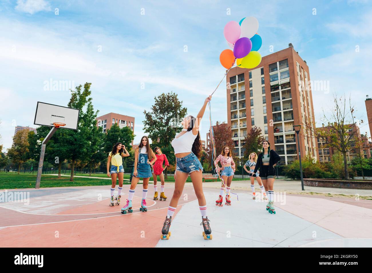 Happy woman wearing roller skates holding colorful balloons in front of ...
