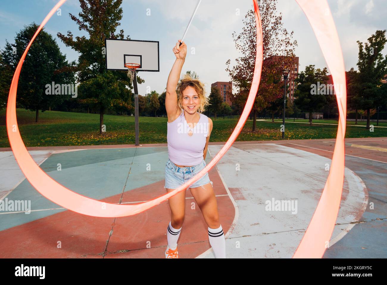 Happy woman dancing with ribbon and roller skating at sports court ...