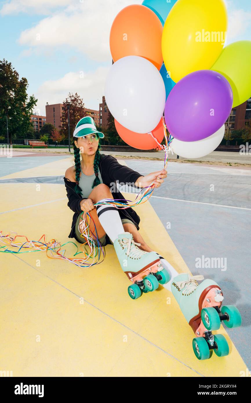 Woman wearing roller skates holding colorful balloons at sports court ...