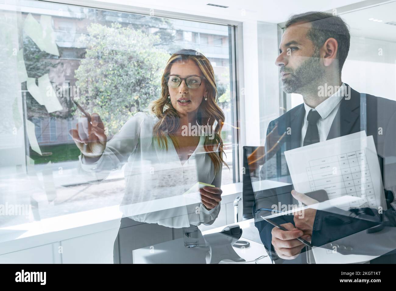 Businesswoman explaining to colleague using sticky notes in office ...
