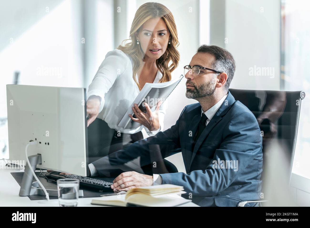 Businesswoman explaining colleague over computer in office Stock Photo ...