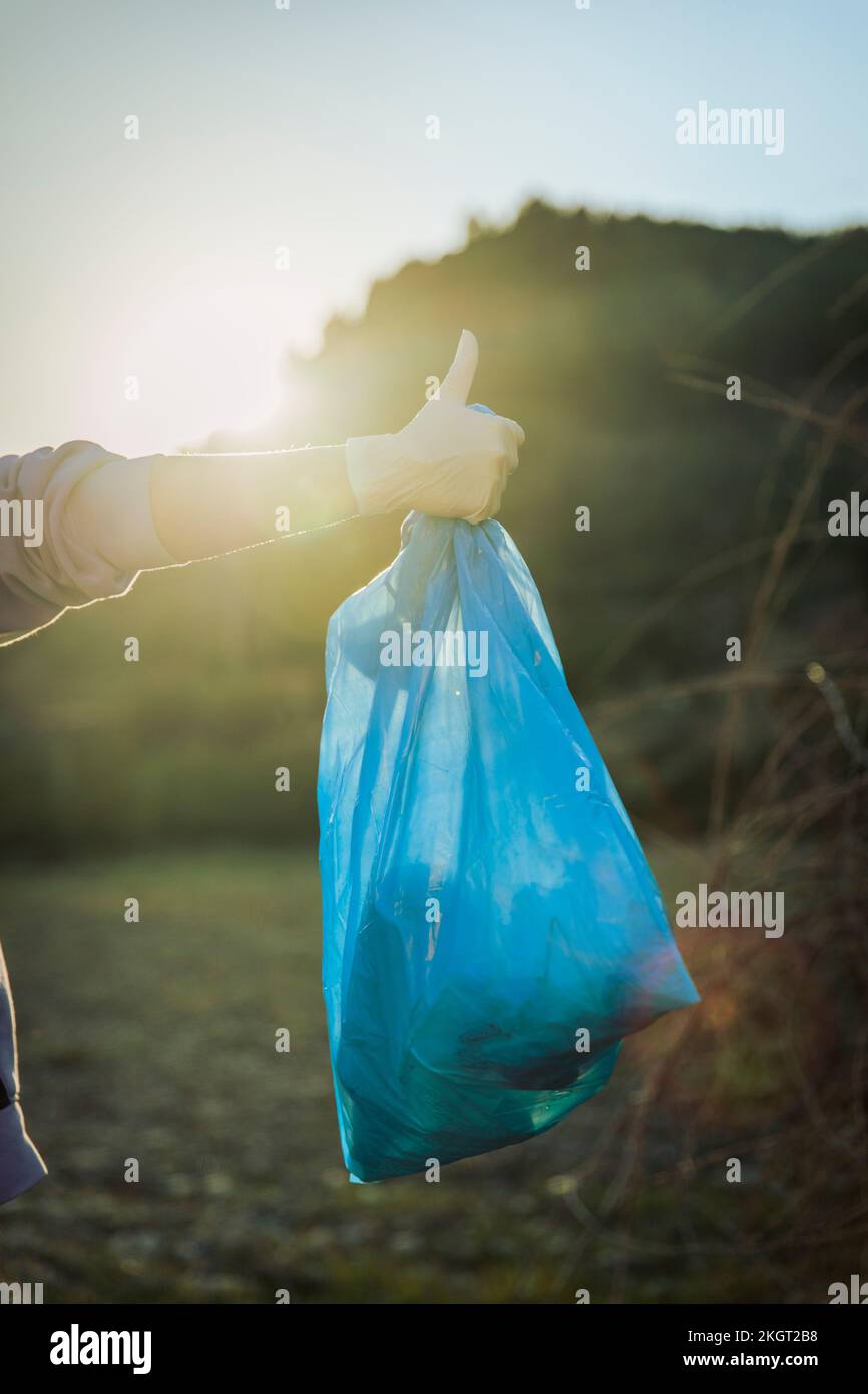 Young woman showing thumbs up gesture holding blue garbage bag on ...