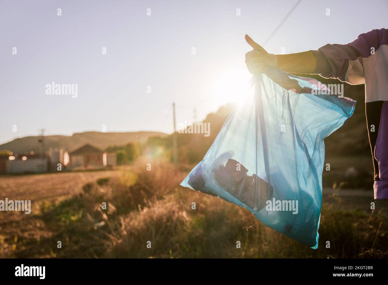 Woman holding garbage bag showing thumbs up gesture on sunset Stock ...