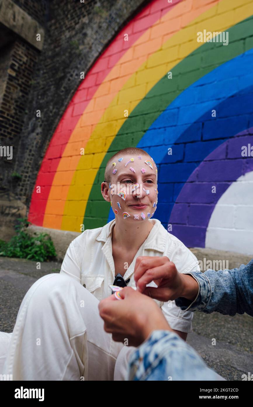 Non-binary person with sticker on face sitting by friend in front of ...