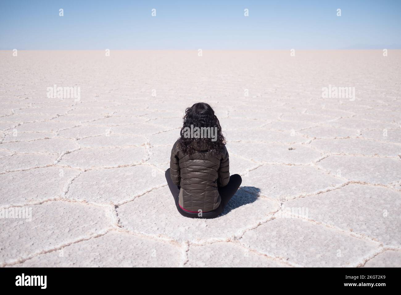 She is sitting with a blurred background on the peculiar salty ground ...