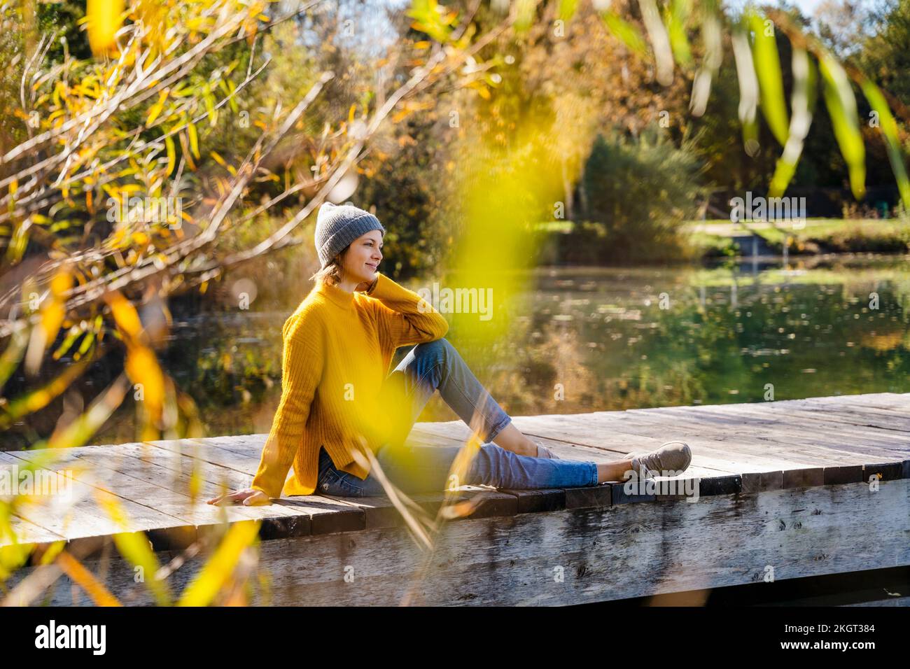 Smiling woman wearing knit hat sitting on jetty Stock Photo - Alamy