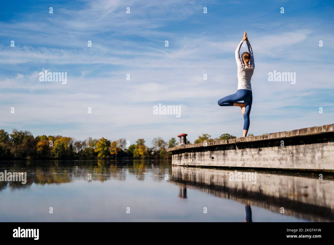 Woman practicing tree pose on jetty under sky Stock Photo - Alamy