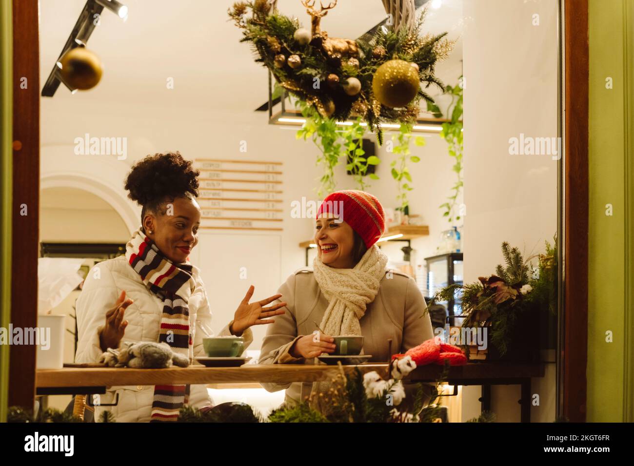 Happy friends talking to each other sitting in cafe seen through glass ...