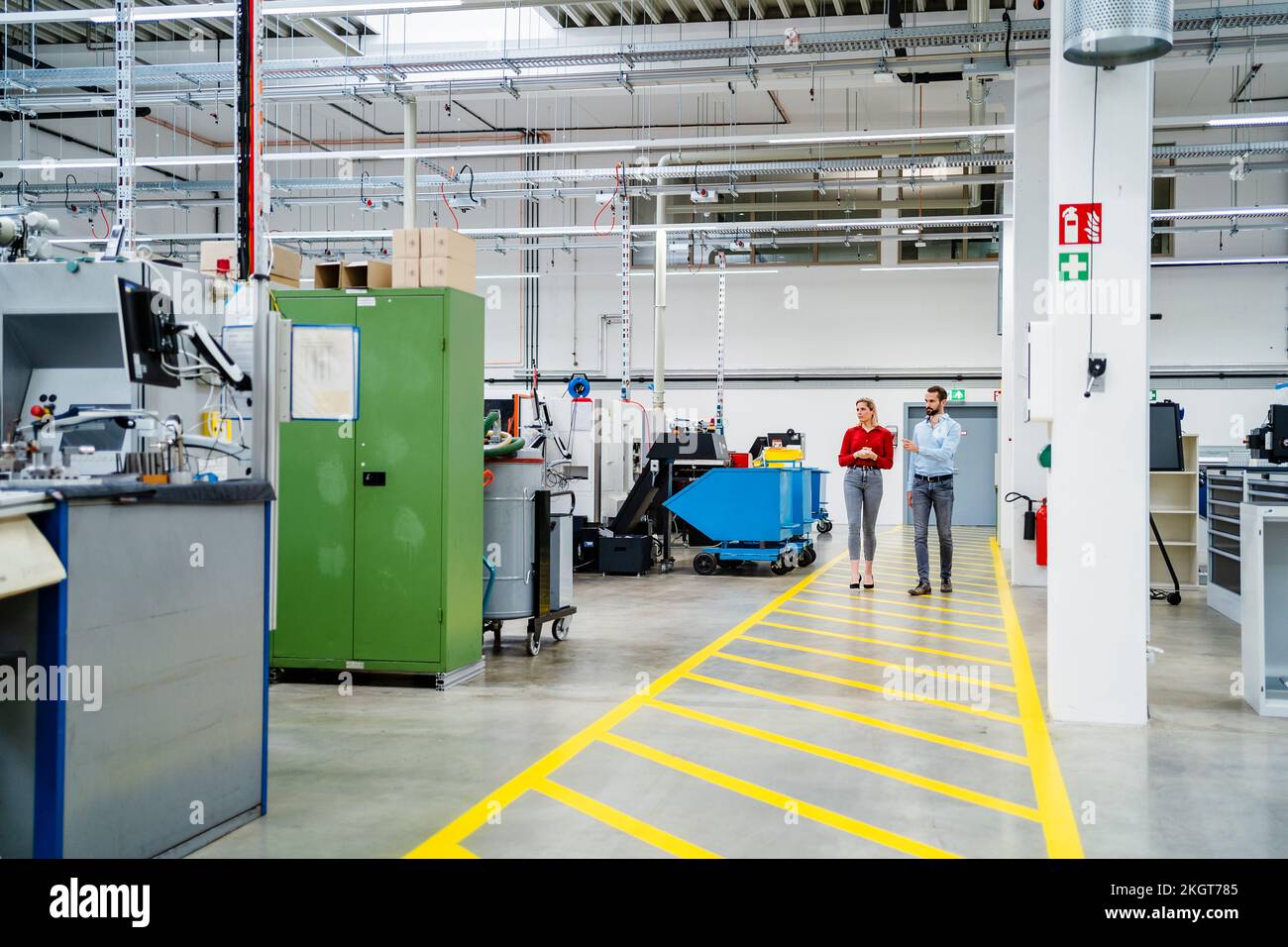 Business colleagues walking together on markings in production hall at ...