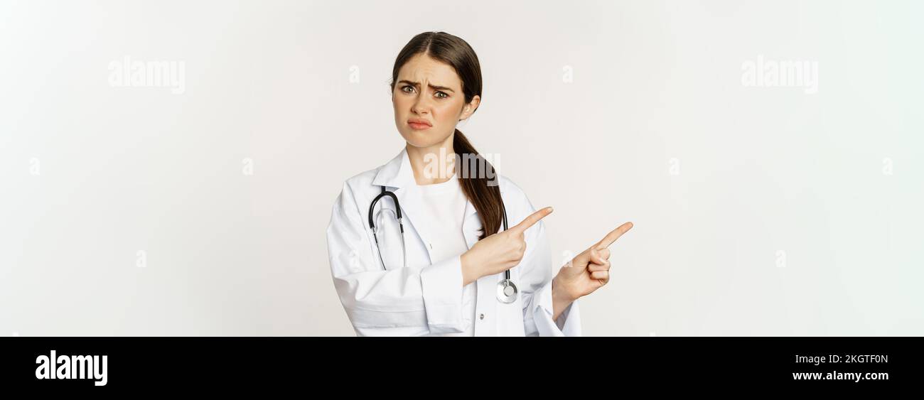 Sad and disappointed female doctor, frowning frustrated, pointing ...