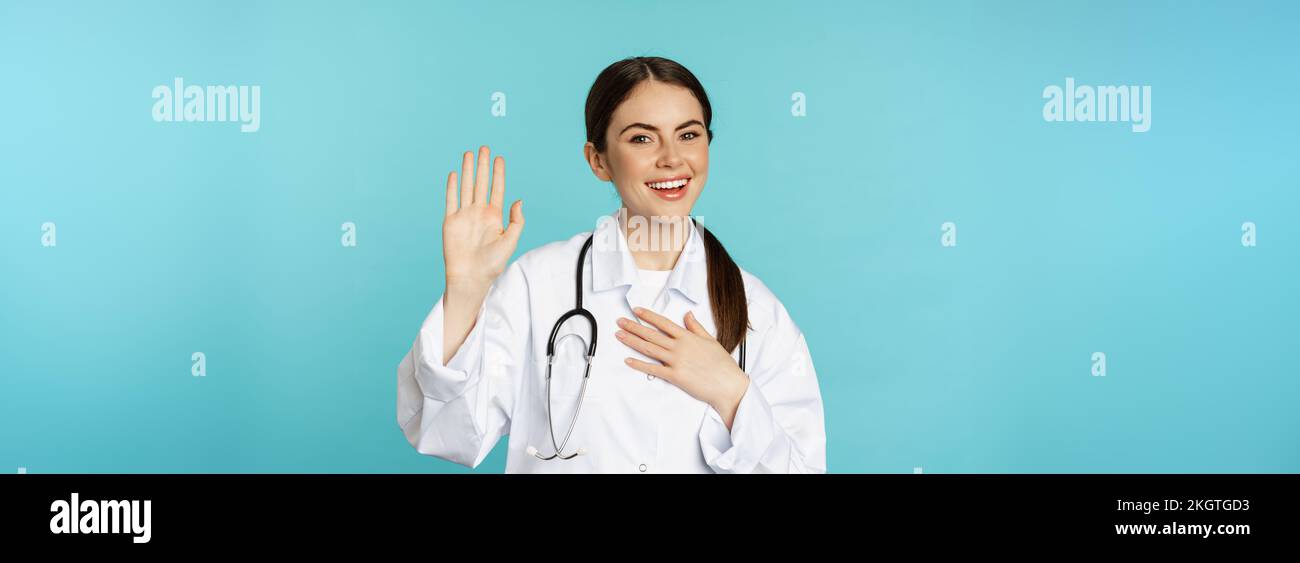 Friendly smiling woman doctor raising hand, name herself, introducing ...