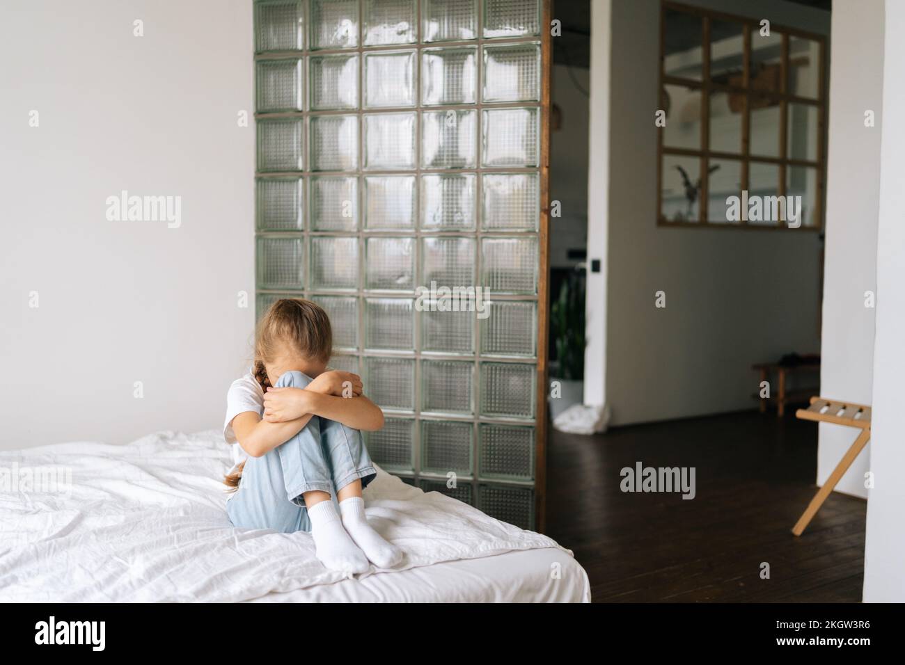Sad unrecognizable little girl hugging knee, sobbing with head bowed ...