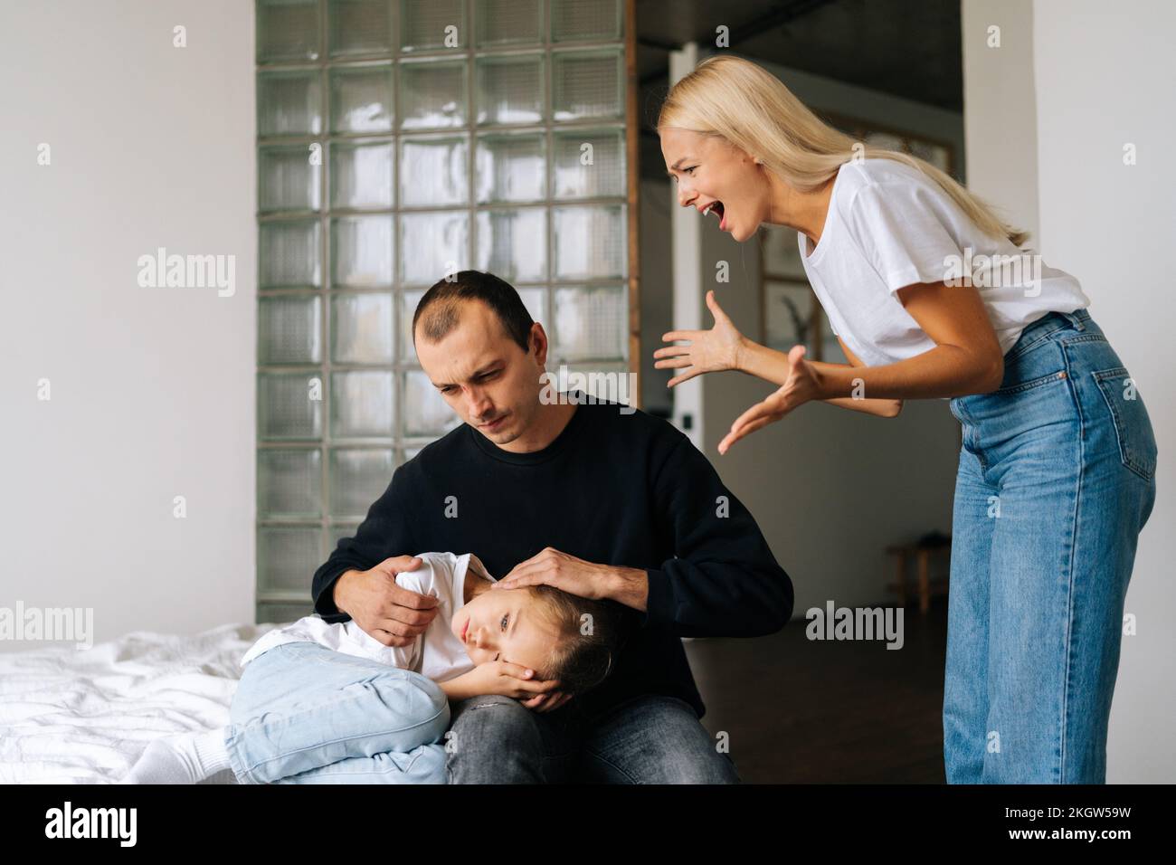 Portrait of scared tired father and daughter hugging each other sitting on bed while aggressive ...