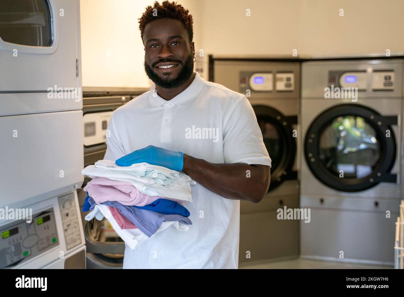 Contented guy standing among washing machines in a laundry facility ...