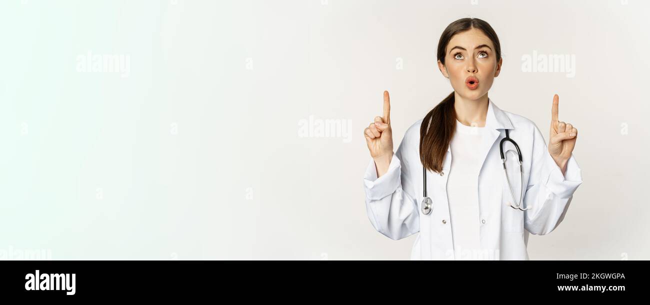 Happy beautiful doctor, female physician pointing fingers up, showing ...