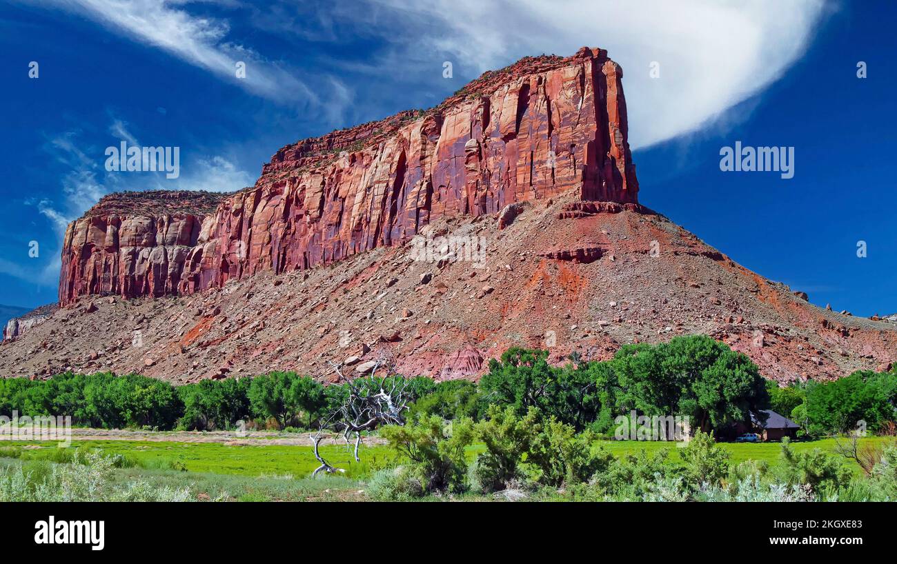 Green valley with steep red sandstone hill formation (butte) sentinal ...