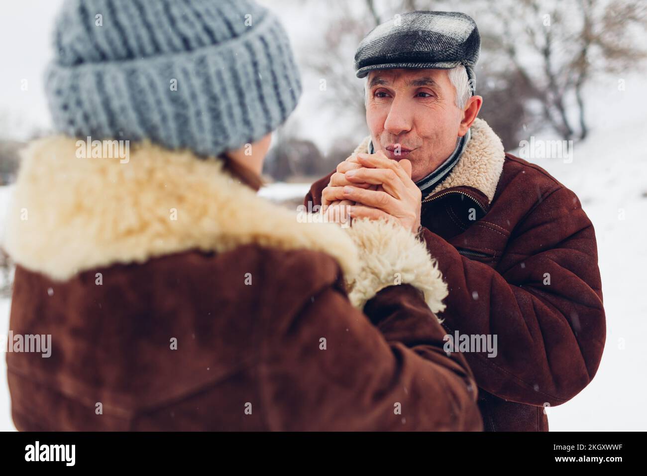 Elderly caring man warms wife's hands with breath outdoor. Senior ...