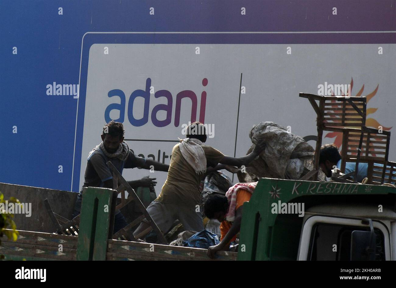 People are seen working on a truck next to the Adani logo on a poster ...