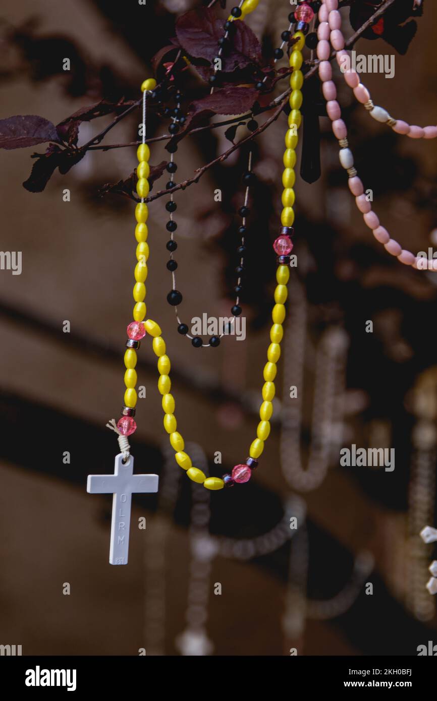 A vertical closeup of yellow Catholic rosary beads hanging from tree ...