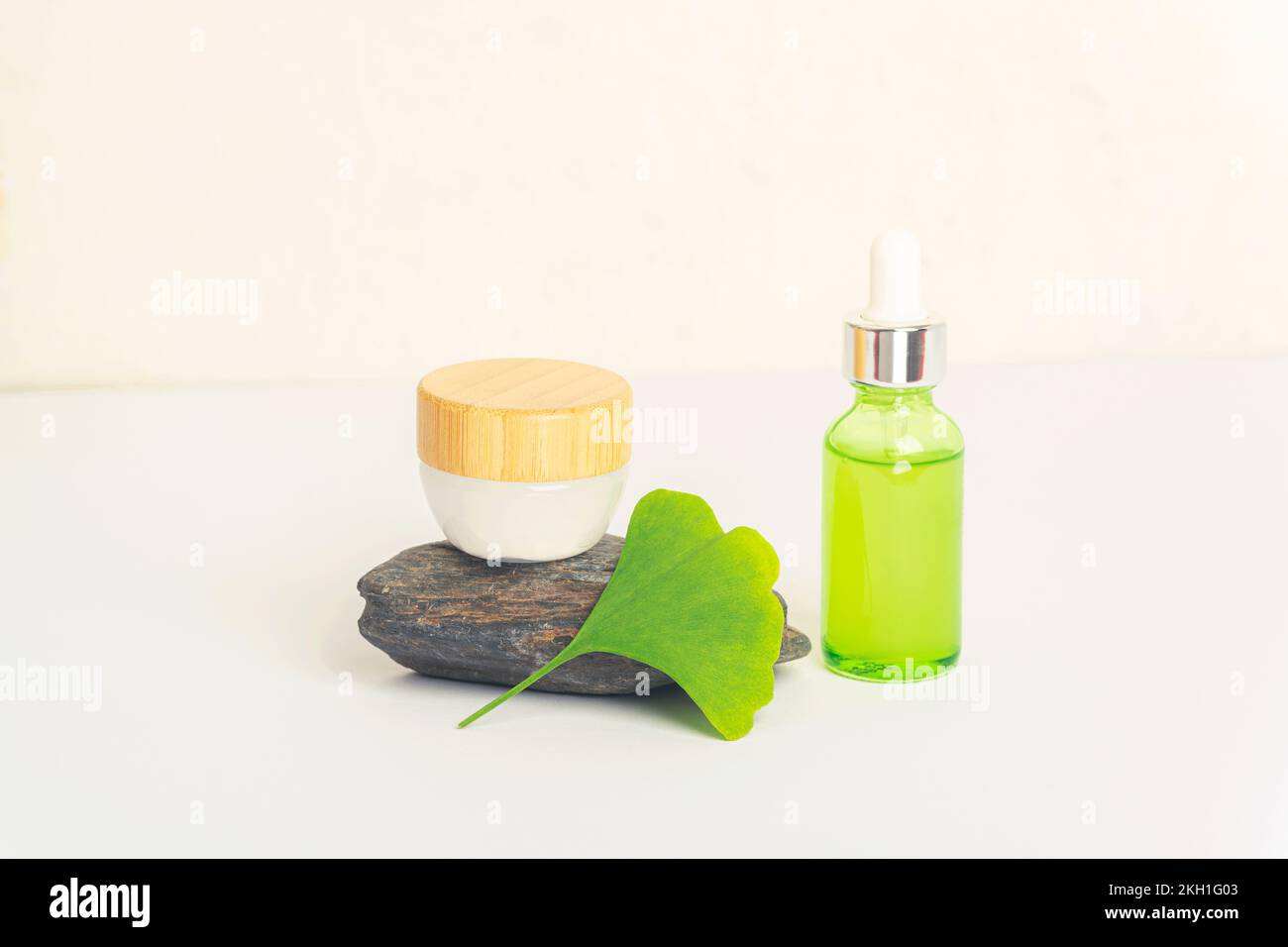Fresh green ginkgo leaf, cosmetic serum bottle and cream jar on white ...