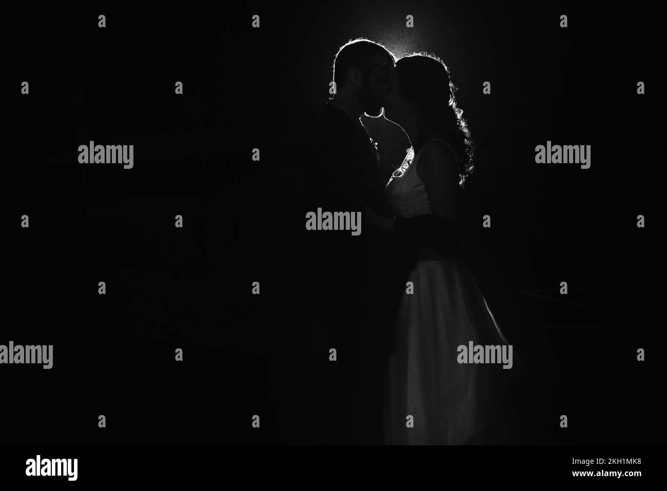 A grayscale of a wedding couple kissing at night against light Stock ...