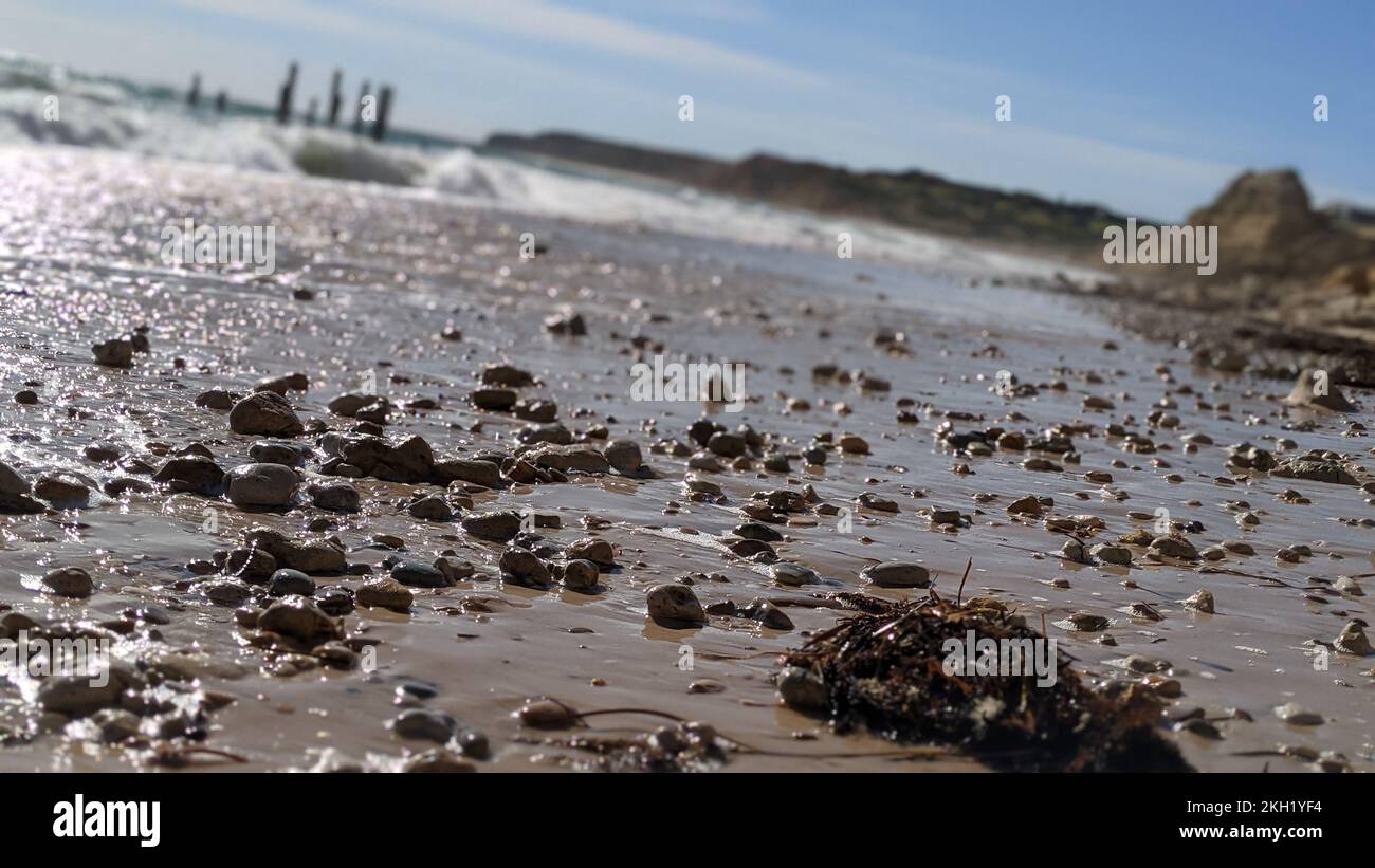A closeup shot of wet pebble stones on a sandy beach on a sunny summer ...