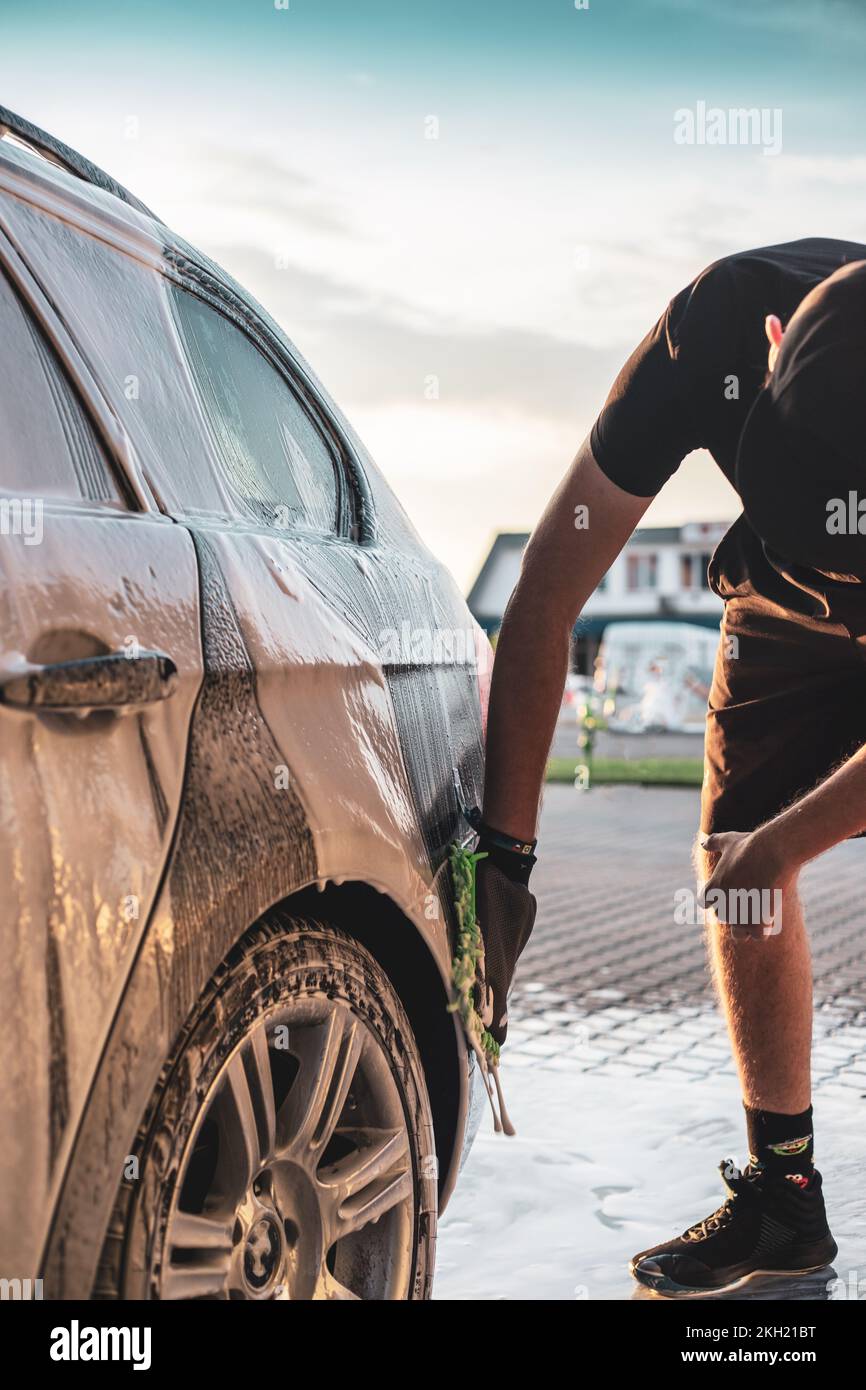 A vertical shot of a man washing his car. A young boy taking care of ...