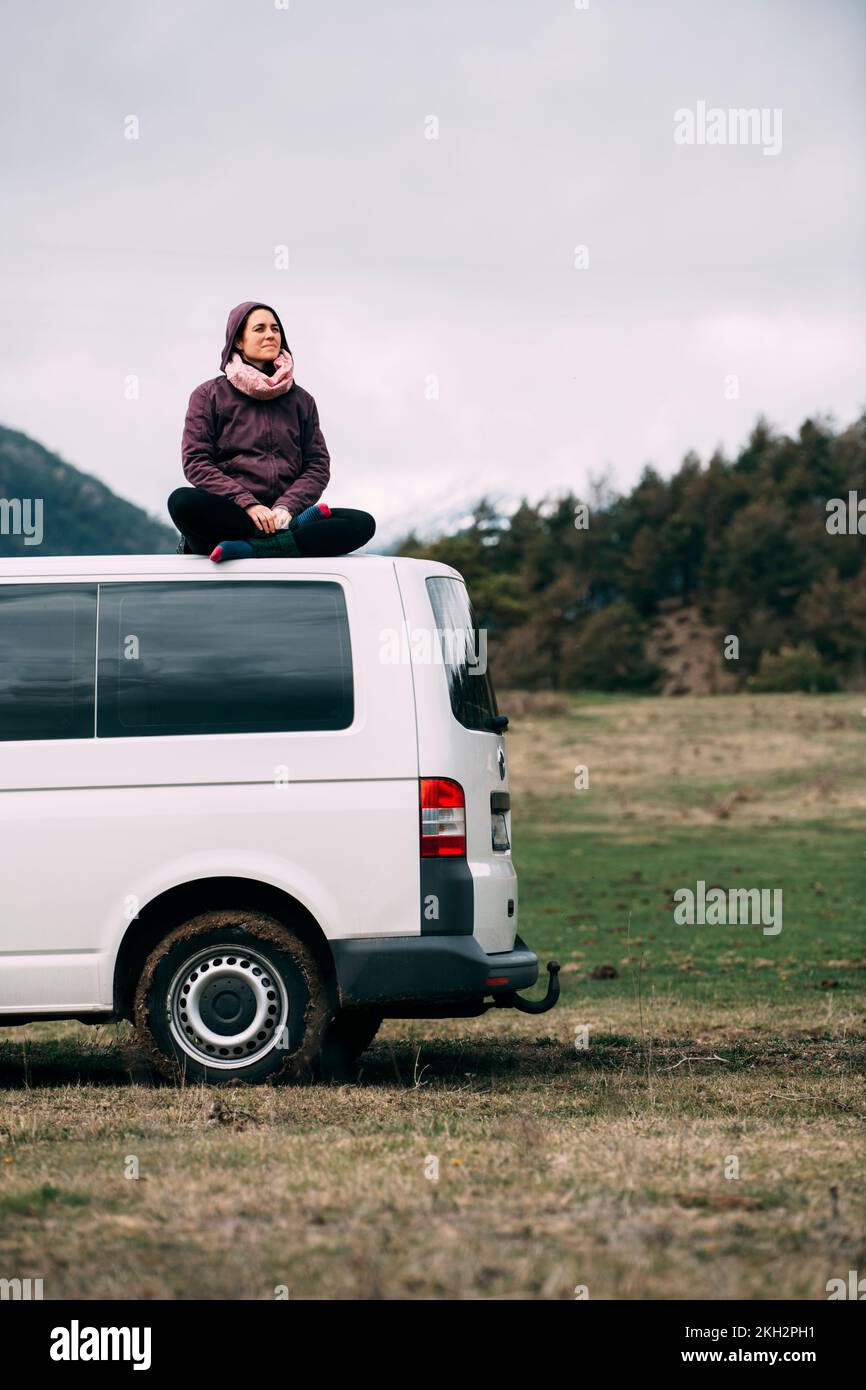 A woman sitting on the roof of a camper van in the forest against a ...