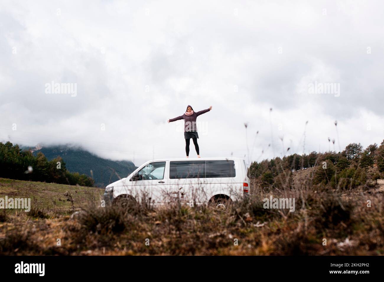 A woman standing on the roof of a camper van in the forest against a ...