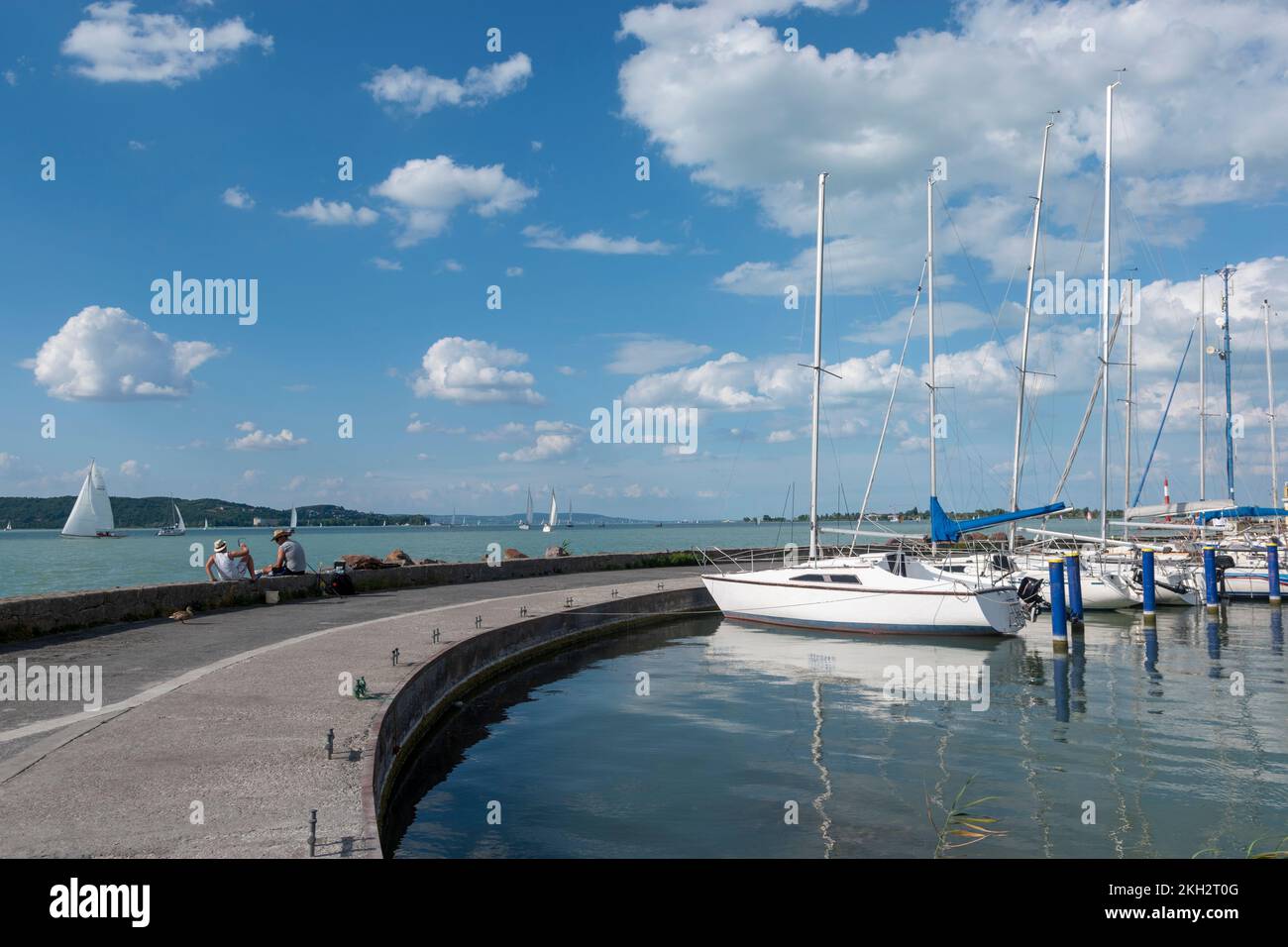 Wooden jetty leading to a port filled with sailing boats at the beach ...