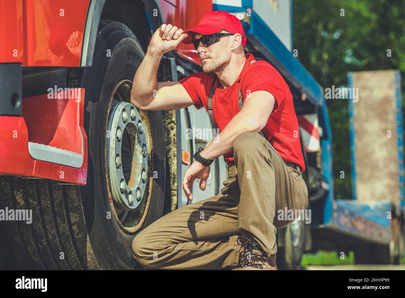 Professional Trucker Resting Next To His Red Semi Truck During Scheduled Driving Rest Stop