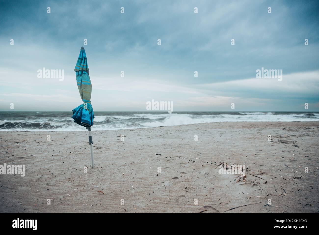 A closed beach umbrella with white foamy waves and sky in background ...