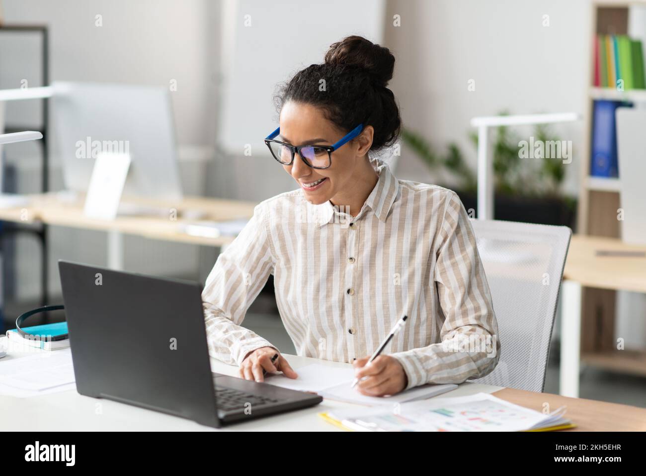 Happy young latin businesswoman working in office, sitting at workplace ...
