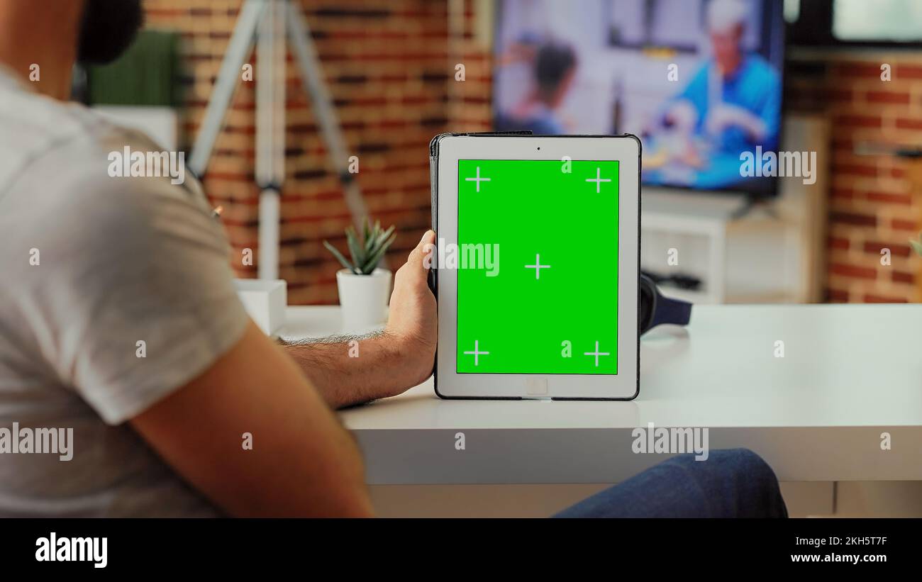 Male freelancer analyzing greenscreen on modern tablet at home, holding ...