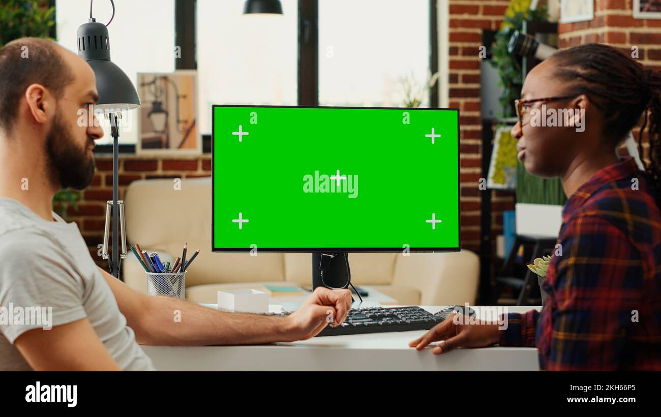 Multiethnic team of people looking at computer with greenscreen ...