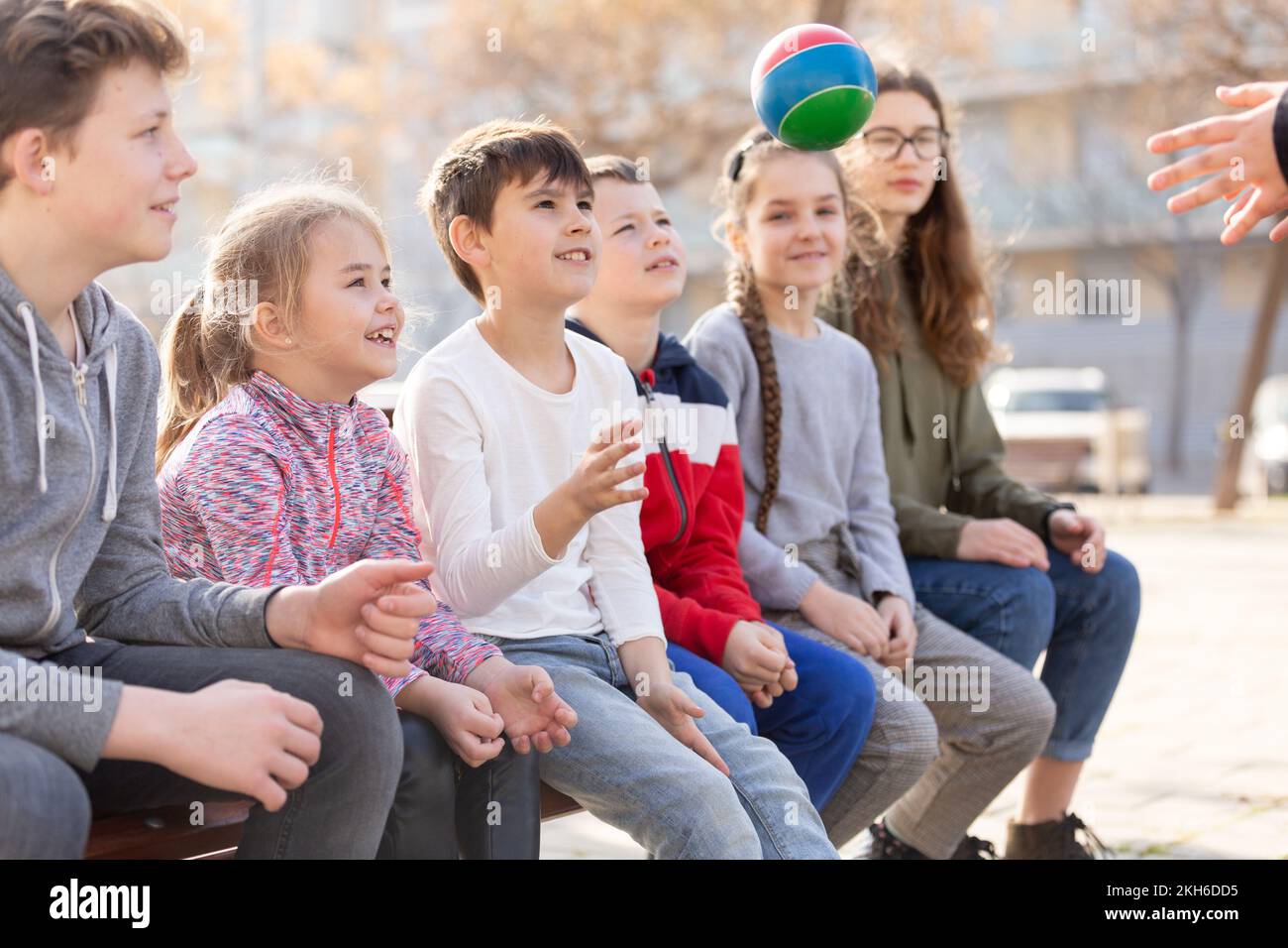 Group of cheerful children relaxing on bench on playground, playing ...