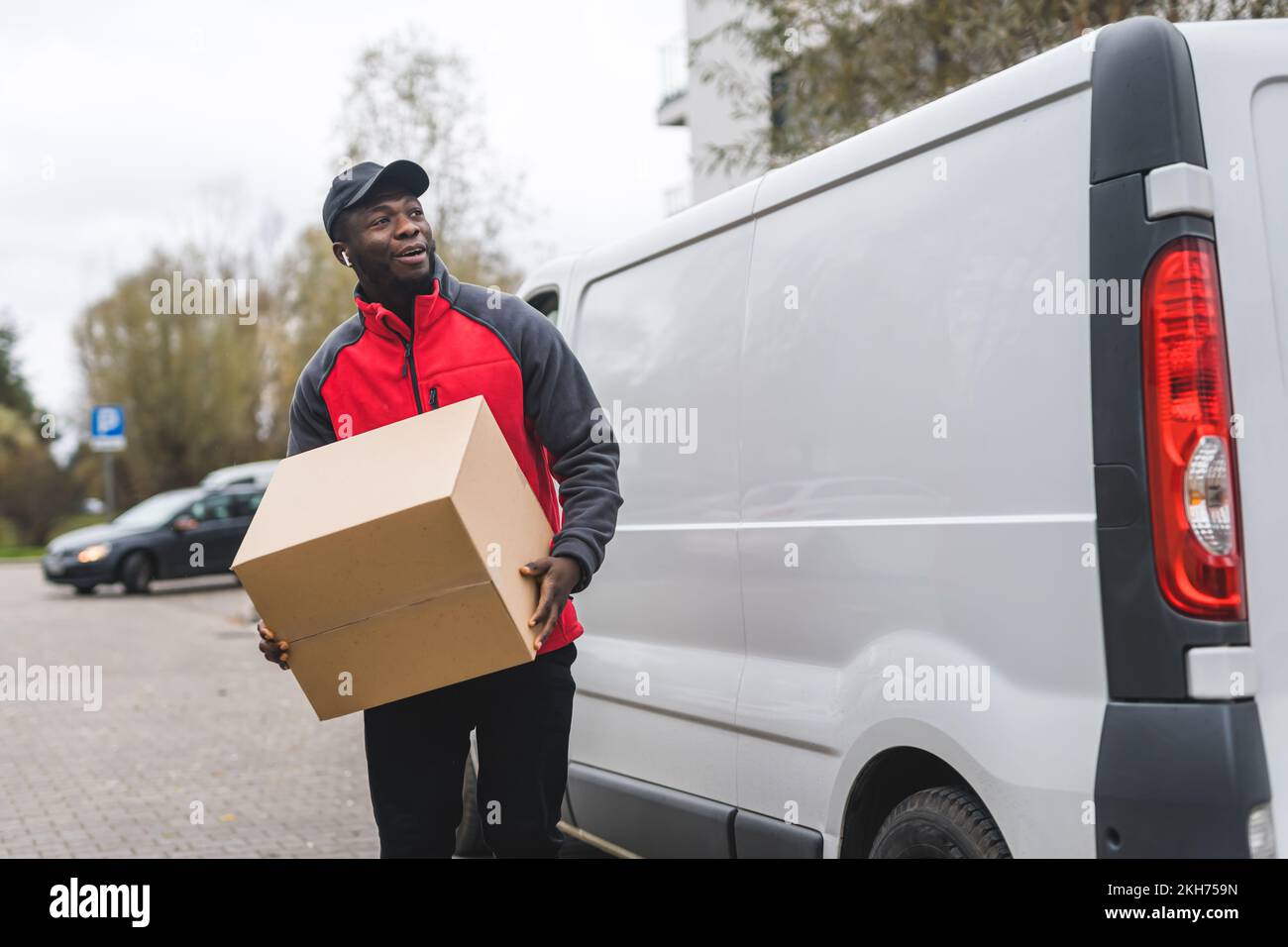 Young adult black delivery guy walking holding cardboard box parcel ...