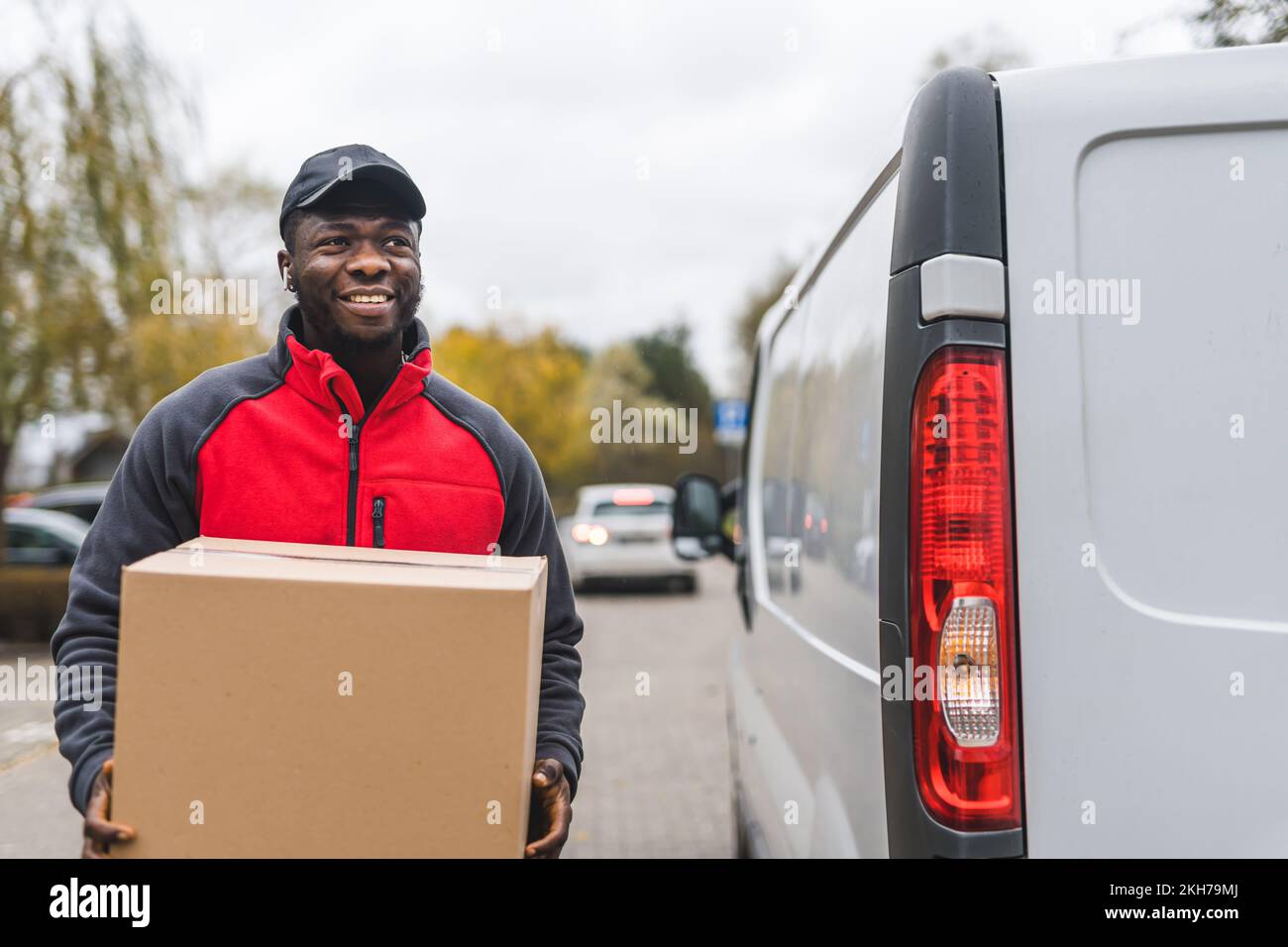 Black young adult delivery man wearing work uniform smiling carrying ...